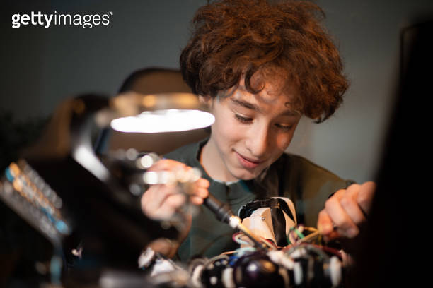 Close-up soldering, young teenager fixes cables,robot wires, small smoke rises from heated ...