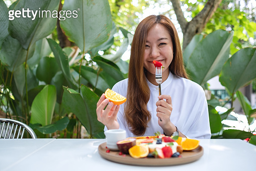 Portrait image of a young woman eating mixed fruits french toast brunch ...