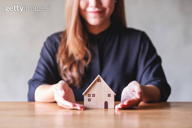 Closeup image of a young woman holding and showing a wooden house model ...
