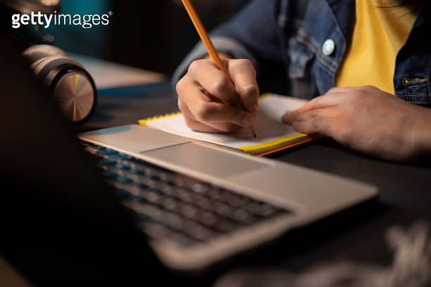 Close-up of girl's hands taking notes with pencil in notebook, laptop ...