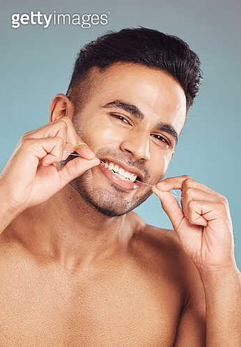 Portrait of one smiling young indian man flossing his teeth against a blue studio background ...