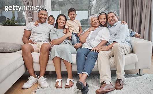 Happy and affectionate young mixed race family of seven sitting on a sofa in the home living ...