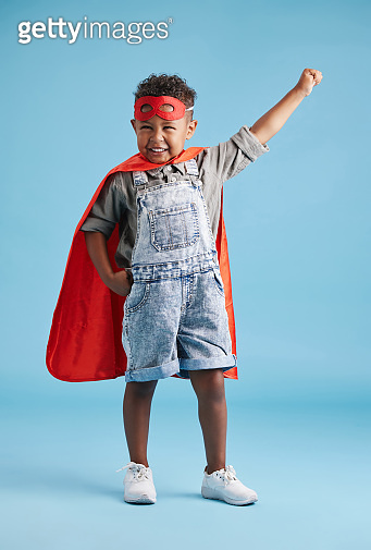 Portrait of cheerful little boy in superhero cape and mask stretching ...