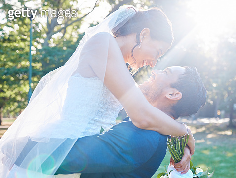Close up of groom lifting bride up while looking into each others eyes on a sunny day in nature ...