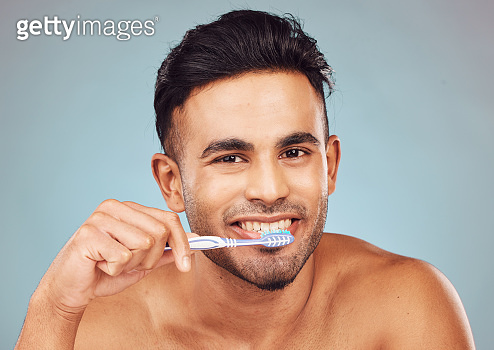 Portrait of one smiling young indian man brushing his teeth against a ...