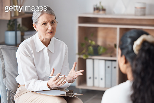 Shot of a mature psychologist sitting with her patient and asking ...