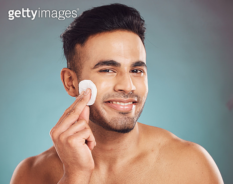 Portrait of one smiling young indian man wiping a round cotton swab on his face while grooming ...