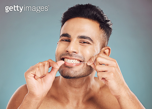 Portrait of one smiling young indian man flossing his teeth against a blue studio background ...