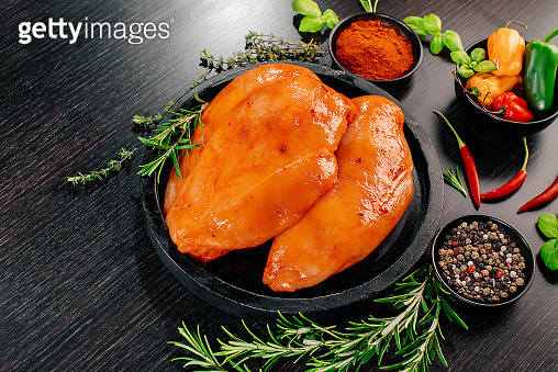 Raw marinated chicken fillet in red sauce on kitchen board on a dark ...