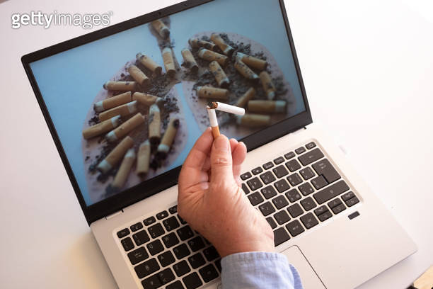 Adult hand holding a broken cigarette over laptop keyboard, ready stop ...