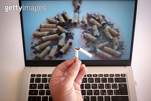 Adult hand holding a broken cigarette over laptop keyboard, ready to ...