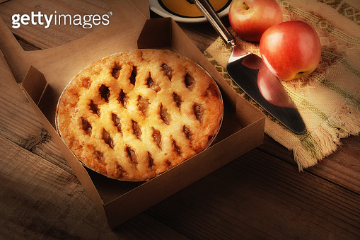 A fresh apple pie in a bakery box on a rustic wood table with plate ...