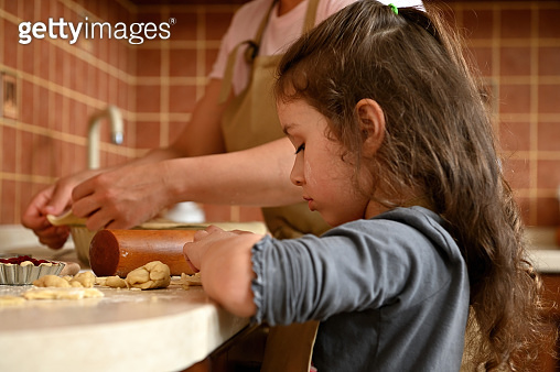 Beautiful European little girl with long hair, using a rolling pin ...