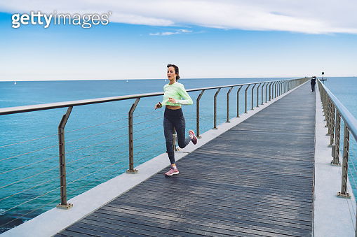 Young female jogger in active clothes reaching running goals on cardio ...