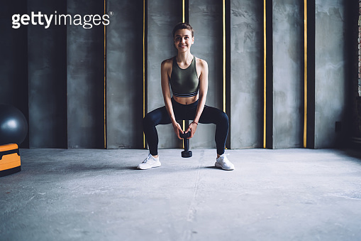Positive caucasian female in active wear squatting with weight training ...