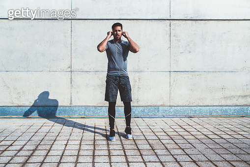 Young confident caucasian sportsman putting on earphones for listening ...