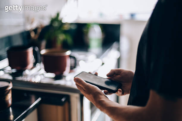 Man using cell phone in the kitchen 이미지 (1388243062) - 게티이미지뱅크