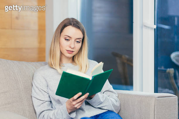 Portrait of a young beautiful woman reading a book, studying, sitting ...