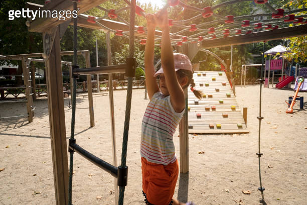 Little girl playing on playground, hanging walk along monkey bars ...