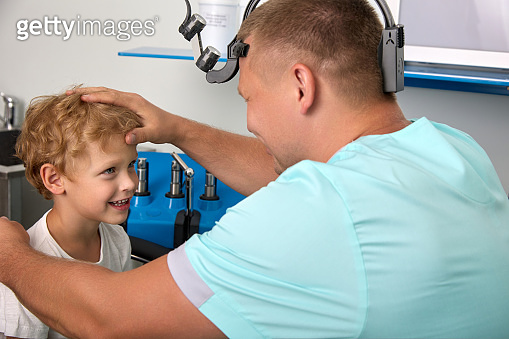 curly cute boy smiles cheerfully at reception at the ENT in children's ...