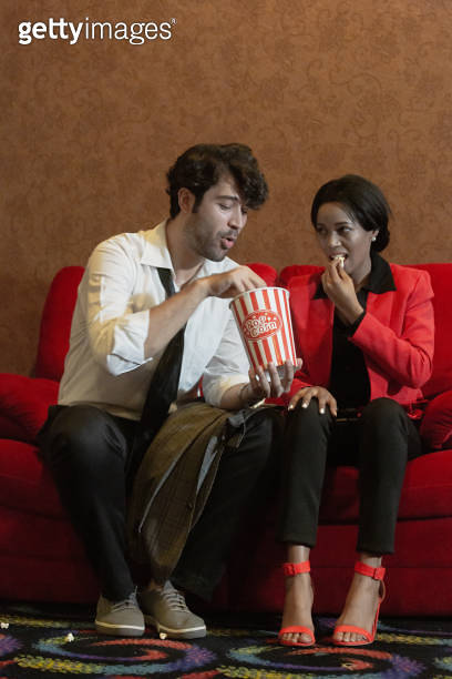 Couple eating popcorn while waiting to get in to cinema for watching ...