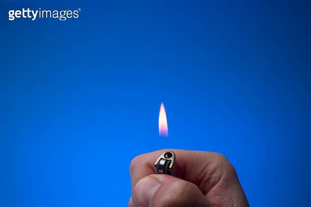 Lit small lighter with flame held between fingers by man. Close up ...