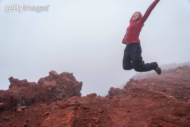 Women jumping up the volcanic rocks of volcano Eldfell eruption ...