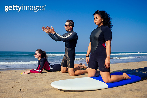 surf instructor and two girls beginner surfers try to stand up on ...