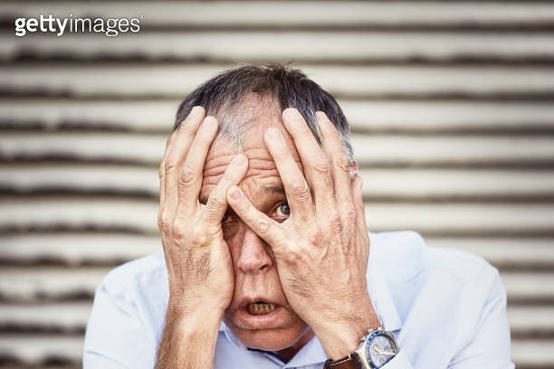 Terrified middle-aged man peeks cautiously through his fingers, full of ...