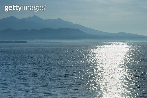 Bright shiny sunrise on sea with blue mountains in haze on horizon ...
