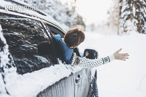 Teenager boy looking out of car window traveling in winter snowy forest ...