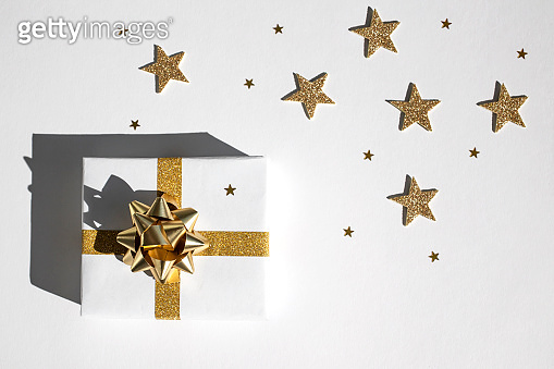 Christmas present in white paper with gold bow and gold stars on white ...