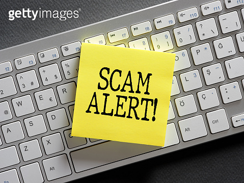 The word scam alert written on a sticky note paper on computer keyboard ...