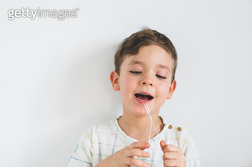Cute boy pulling loose tooth using a dental floss. The boy's first milk ...