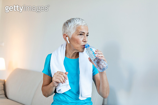 Senior woman holding plastic bottle of water,wiping sweat with a towel ...