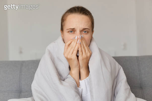 Indoor shot of sick woman with headache sitting under the blanket anf ...