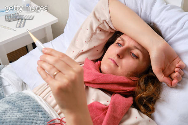 A sick woman with a sore head and a thermometer is lying on the bed ...