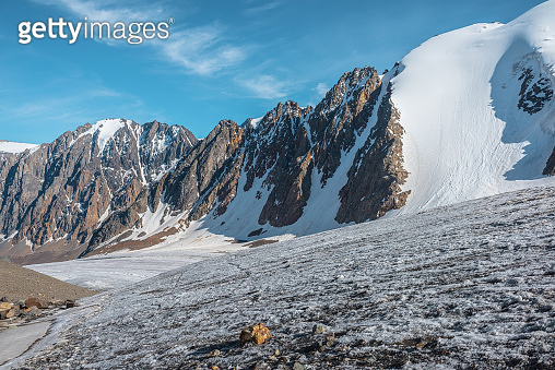 Scenic mountain landscape with glacier under sharp rocks in sunlight ...