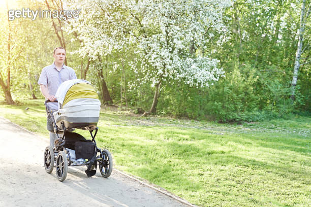 A man with a baby stroller walks through a summer park against the ...