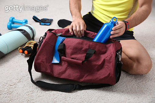 Man packing sports stuff for training into bag on floor indoors ...
