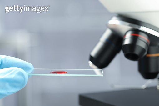 Scientist holding microscope slide with sample of red liquid in ...