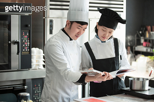 Two young Chinese chefs reading a book on diet and nutrition together ...