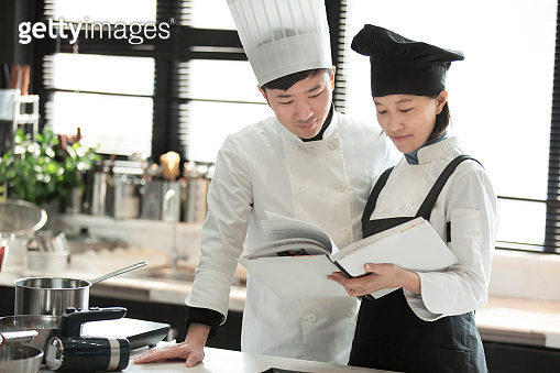 Two young Chinese chefs reading a book on diet and nutrition together ...