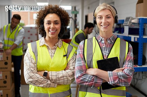 Portrait Of Two Female Workers Using Headsets In Distribution Warehouse ...