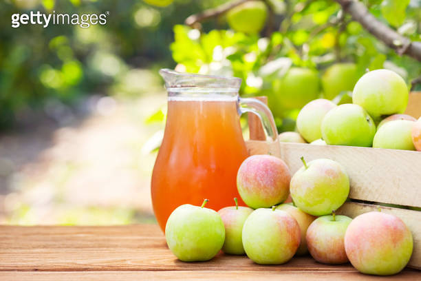Apples, box of apples and pitcher of fresh apple juice on wooden table ...