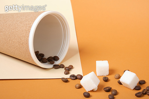 Thermo mug, scattered coffee grains and white sugar cubes on brown and ...