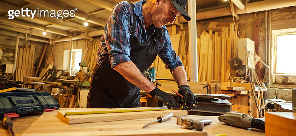 Portrait of a senior carpenter working with a wood, marking plank with ...