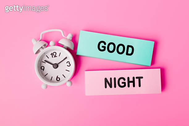 The words Good Night written on paper note near white alarm clock on ...