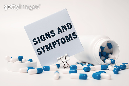 SIGNS AND SYMPTOMS - inscription on paper note near blue-white pills ...