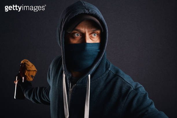 Male activist, rebel, riot wearing hoodie, cap and a face mask holding ...